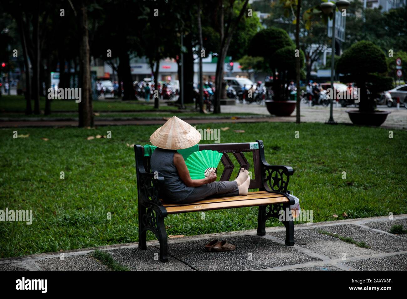 A woman wearing a conical Vietnamese rice hat fans herself on a park ...