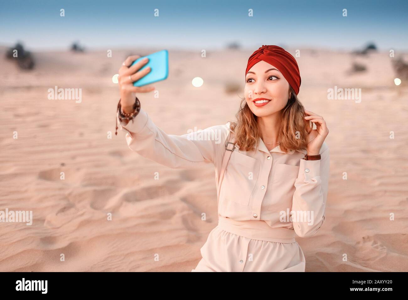 An Asian travel blogger girl in a turban takes a selfie in a sandy ...