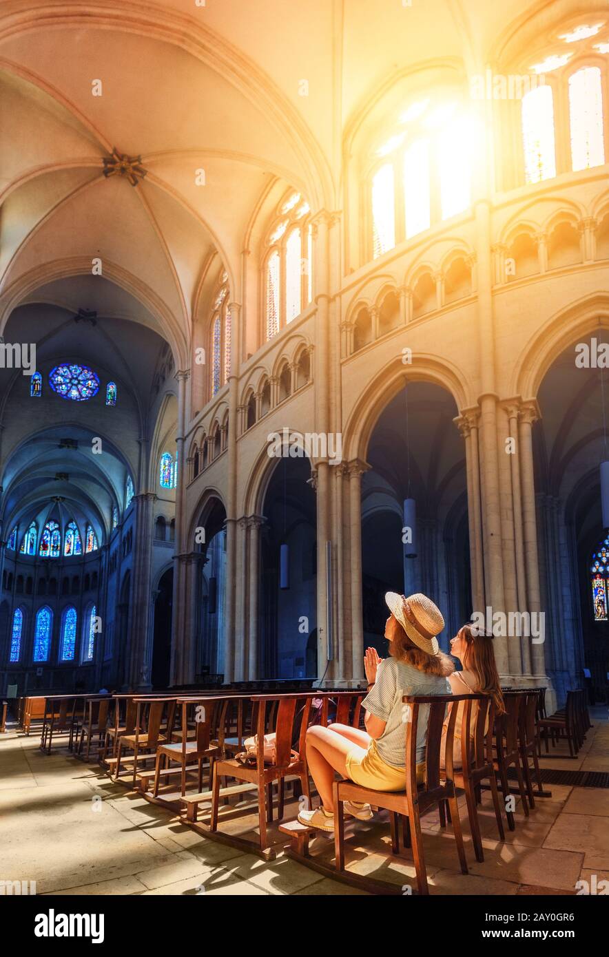 Two faithful girls praying in a church. Sun flare thriugh the window as ...
