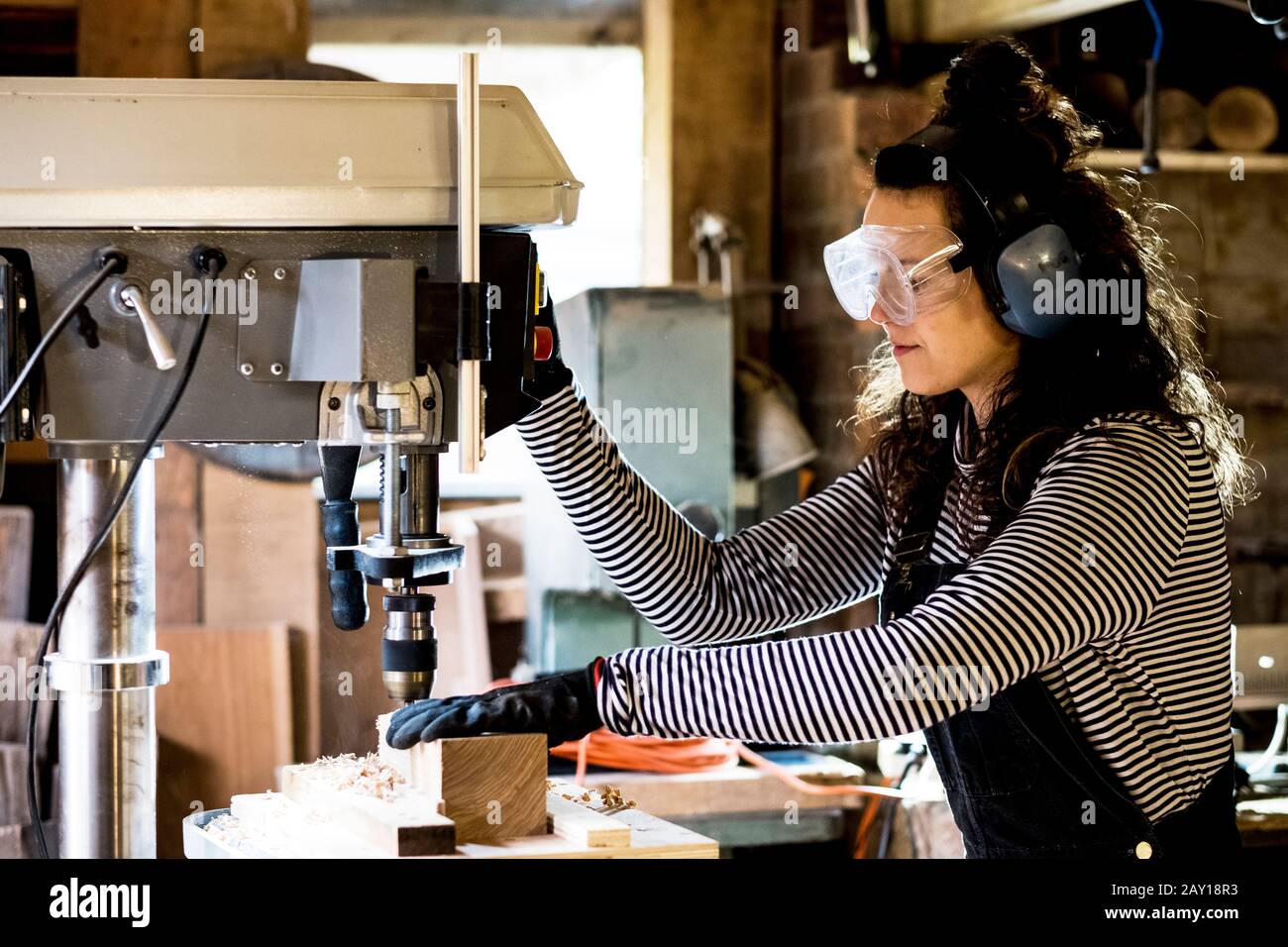 Woman with long brown hair wearing dungarees, safety glasses and ear ...