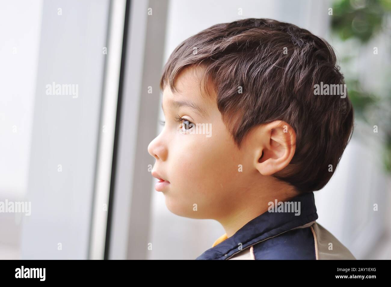 Portrait of little pretty thoughtful boy looking out of the window ...