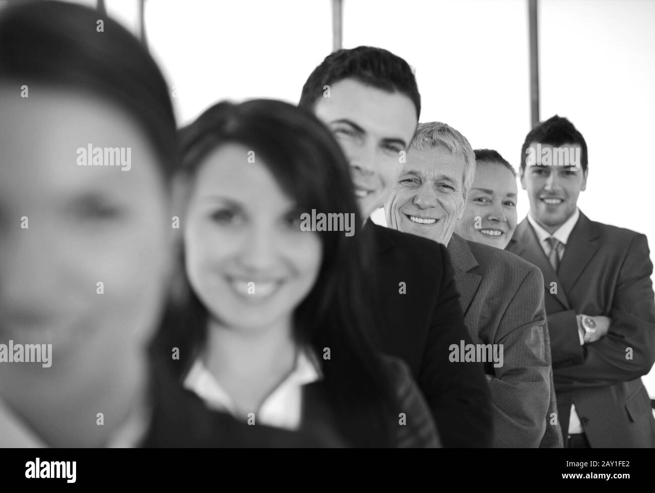 Six cheerful business people standing in a row with their arms folded ...