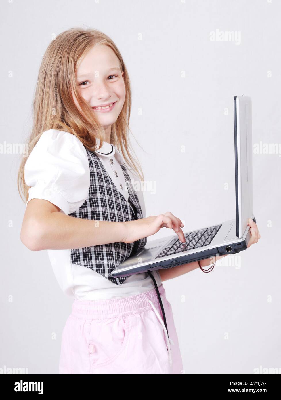 little blond school girl playing on internet standing with laptop ...