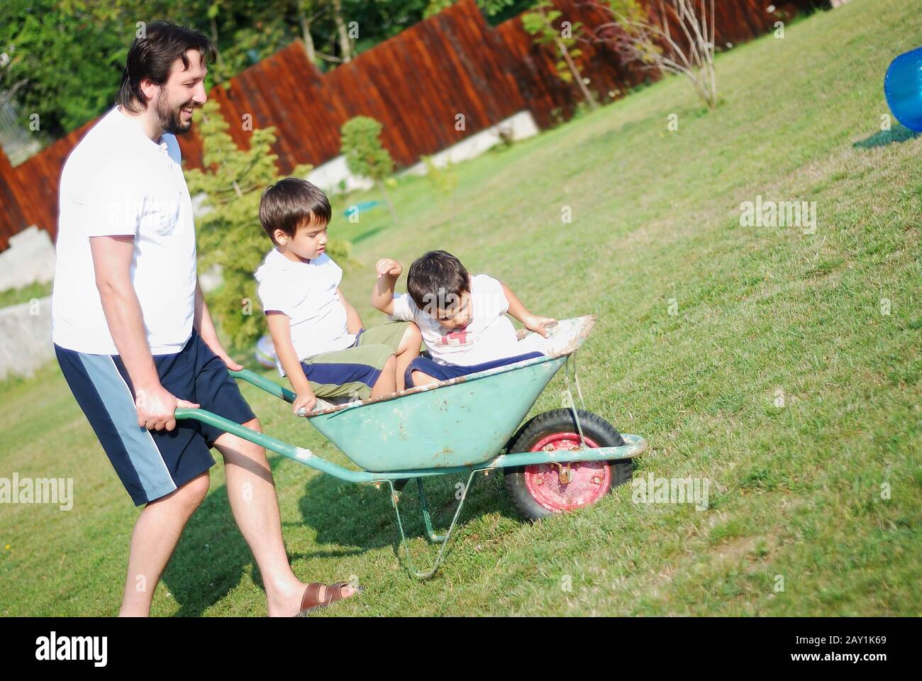 Dad in white driving boys on the wheelbarrow Stock Photo - Alamy