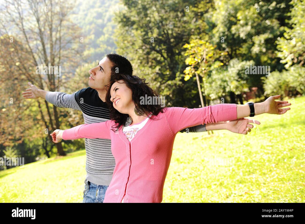 Two young relaxed people in nature with opened arms looking up and ...