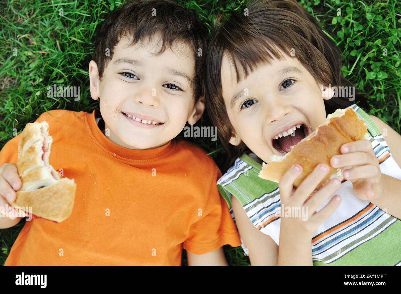 Two cute boys laying on ground in nature and happily eating healthy ...