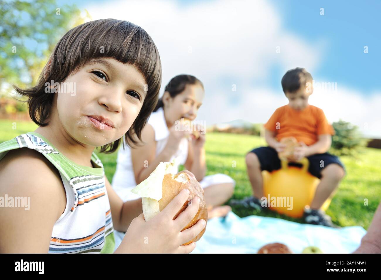 Happy group of children outdoor on meadow: eating and playing together ...