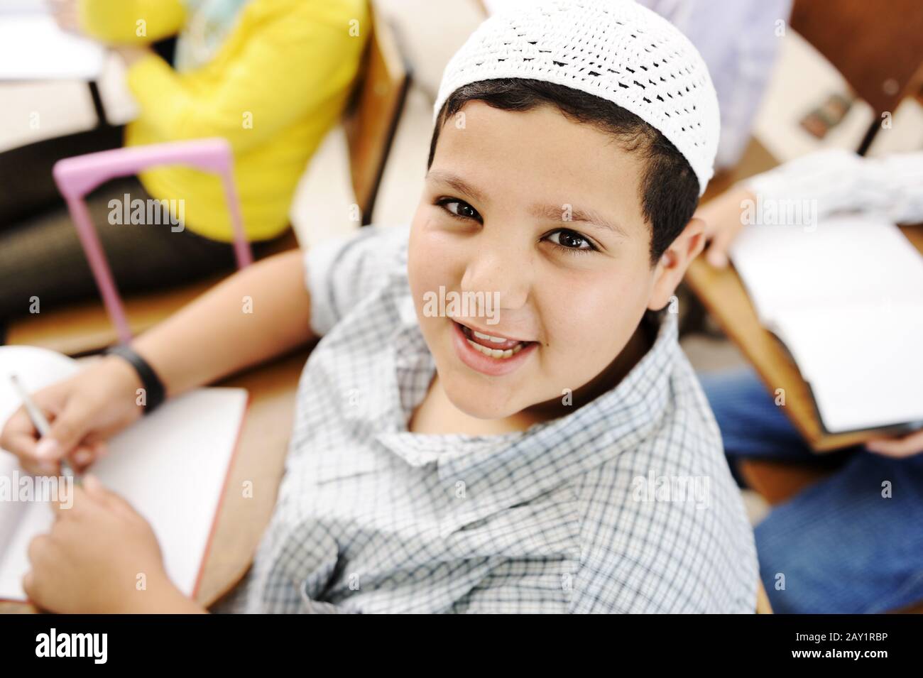 Very positive kid with white small hat sitting on desk in classroom and ...
