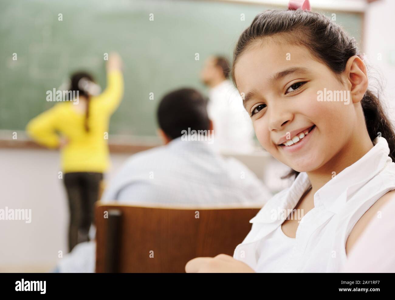 Adorable girl smiling in school classroom and behind her class ...