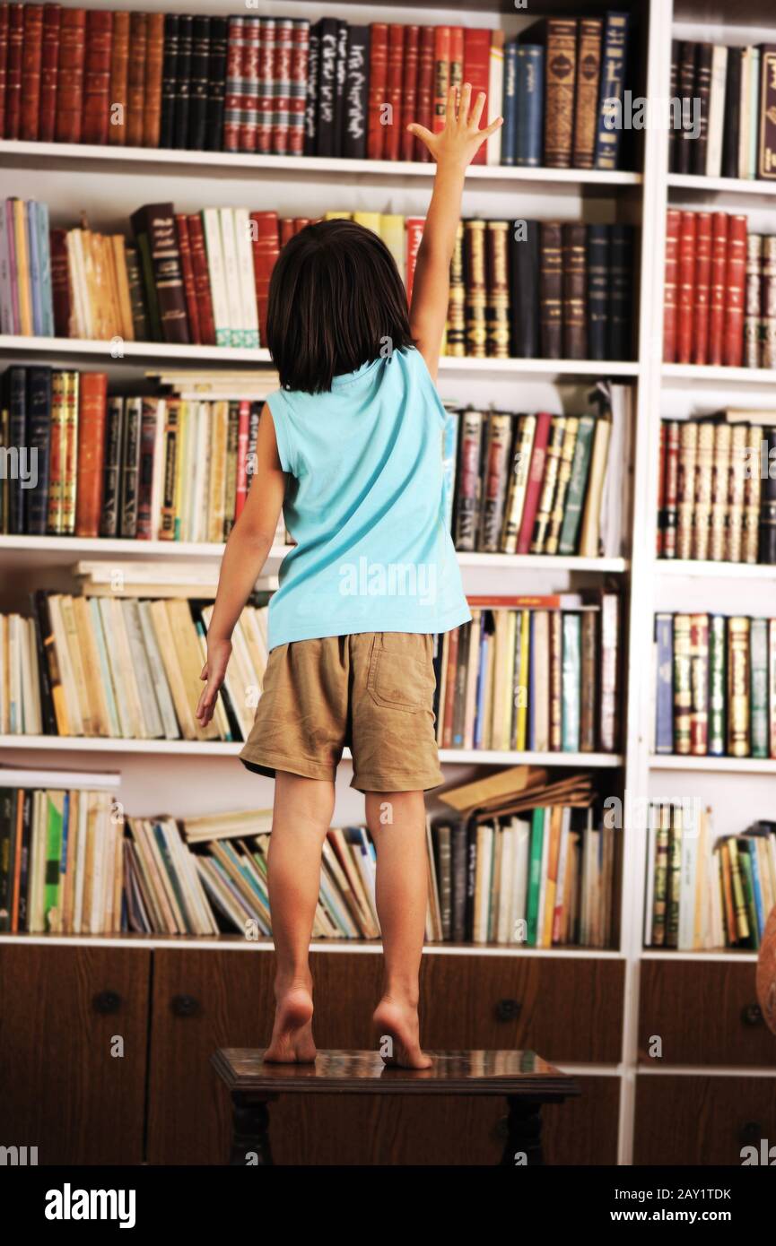 Kid trying to reach a book in the library Stock Photo - Alamy