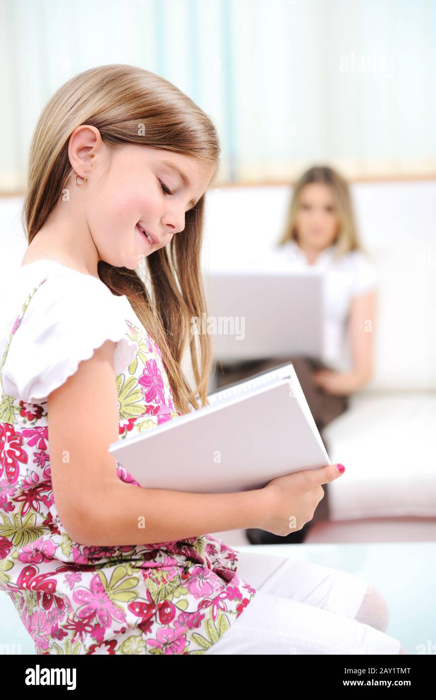 Little girl reading in home with mother Stock Photo - Alamy