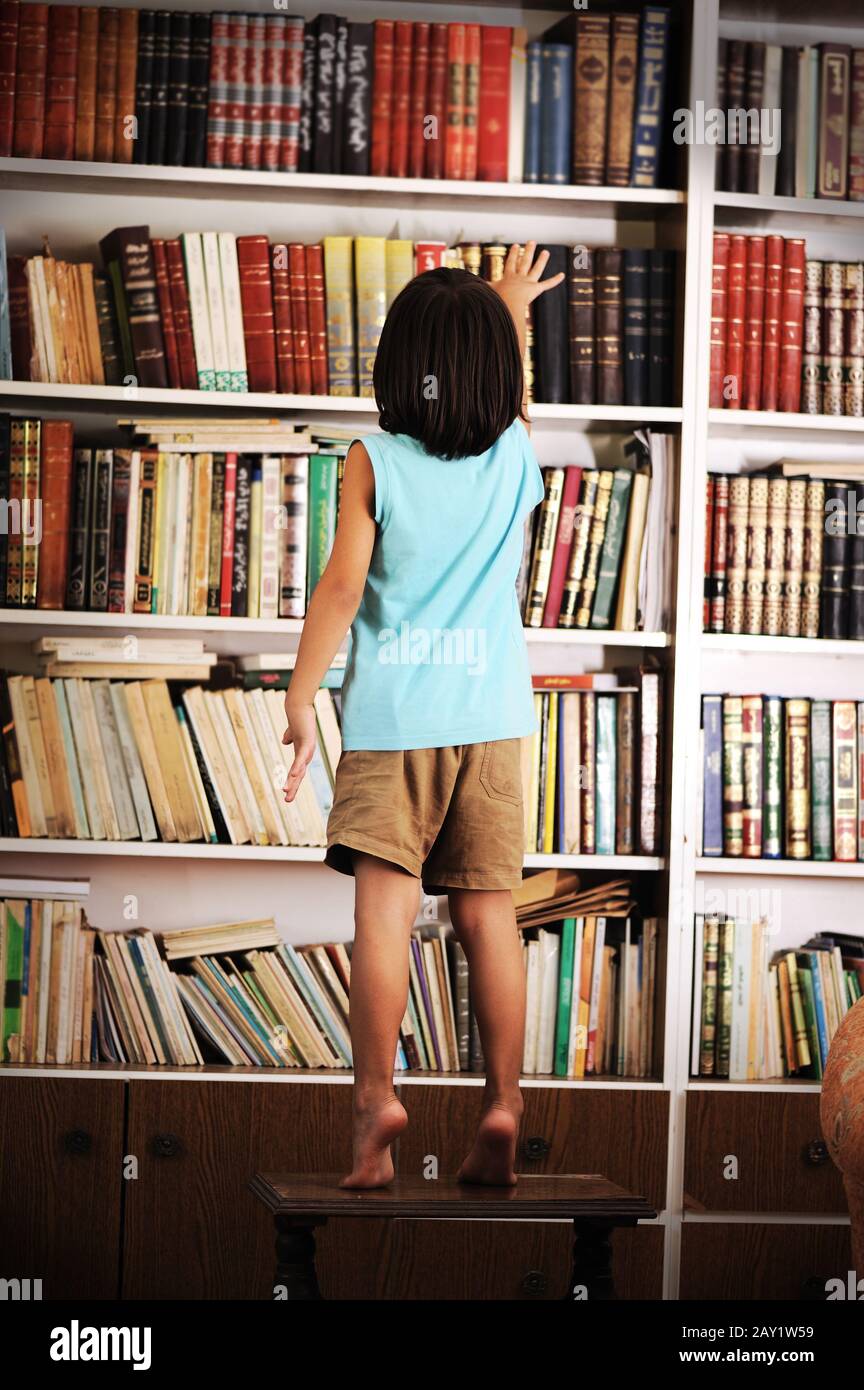 Kid trying to reach a book in the library Stock Photo - Alamy