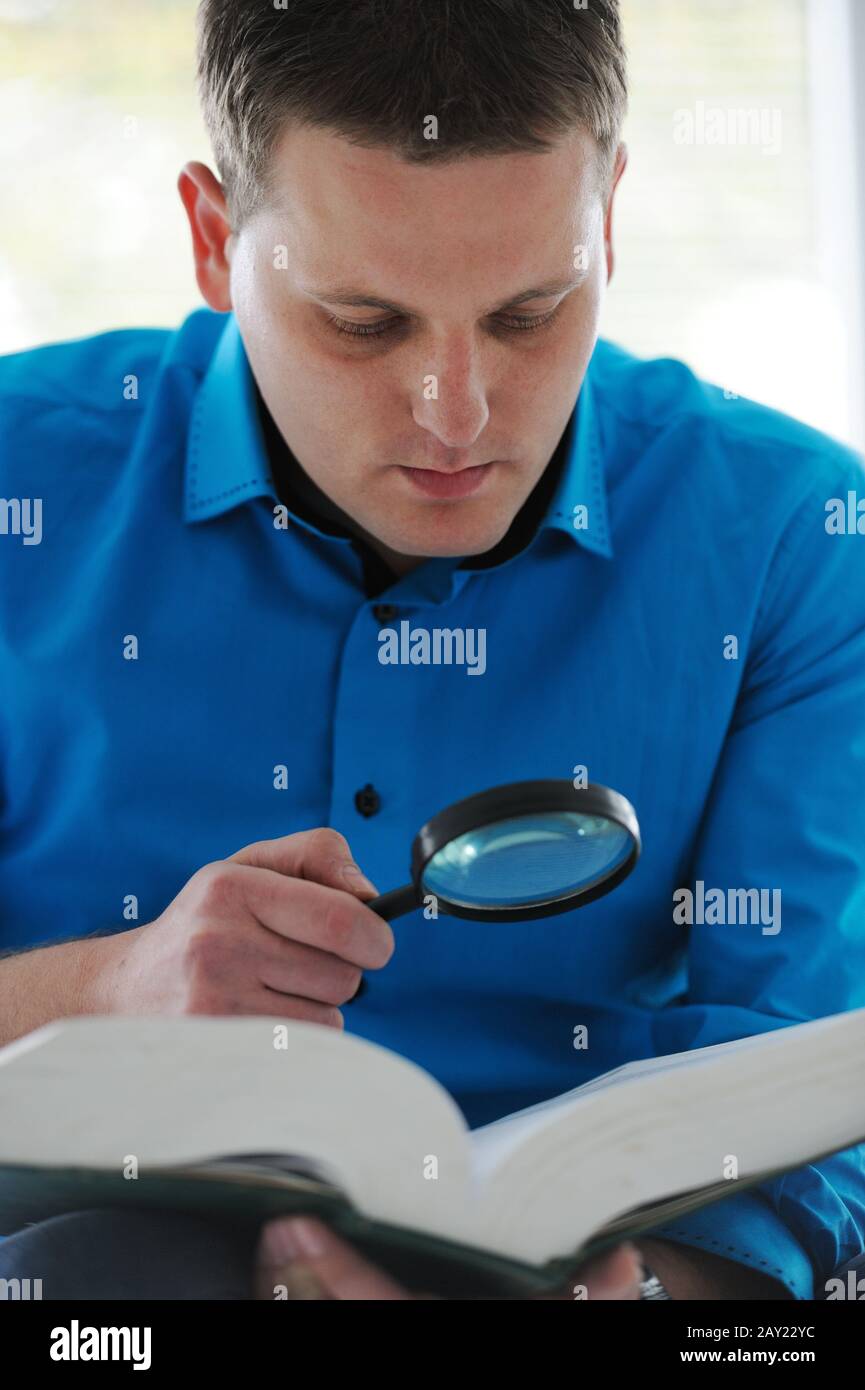 Image of a man reading a book with magnifying glass Stock Photo - Alamy