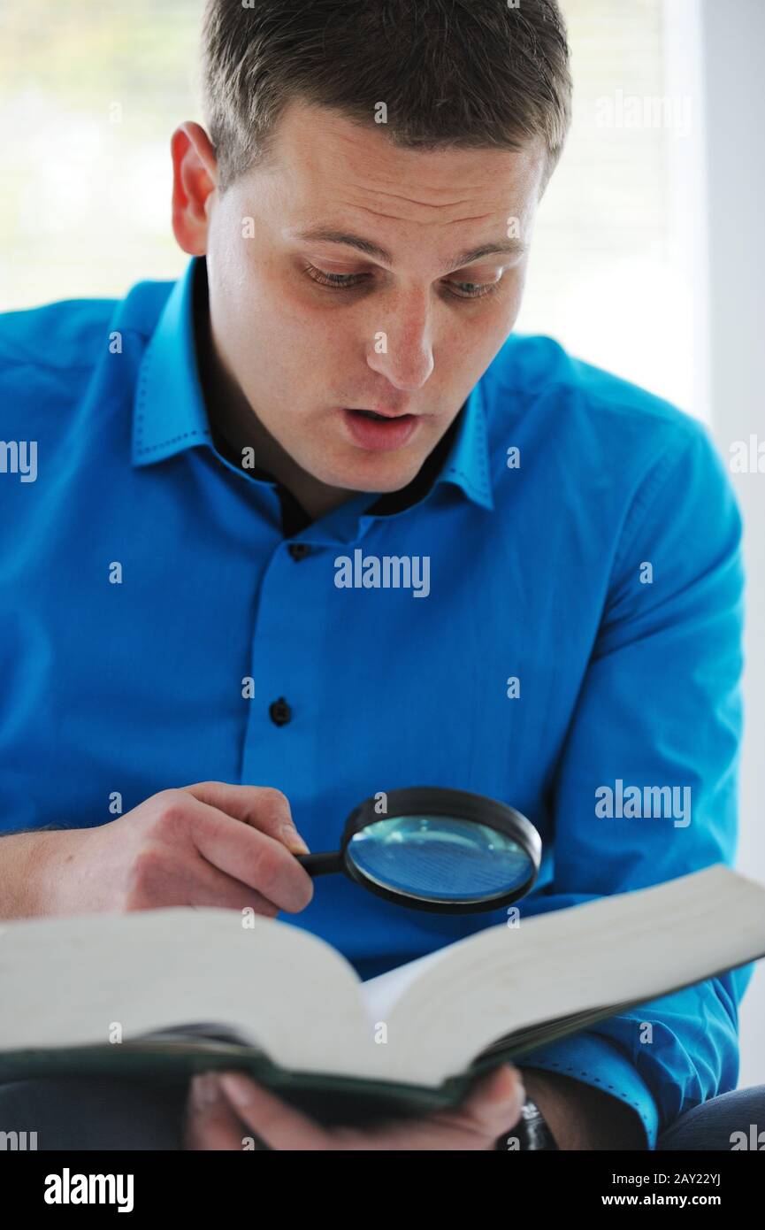 Image of a man reading a book with magnifying glass Stock Photo - Alamy