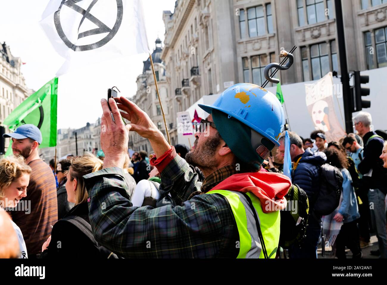 London, UK. A protester with a planet Earth hard hat uses his mobile ...