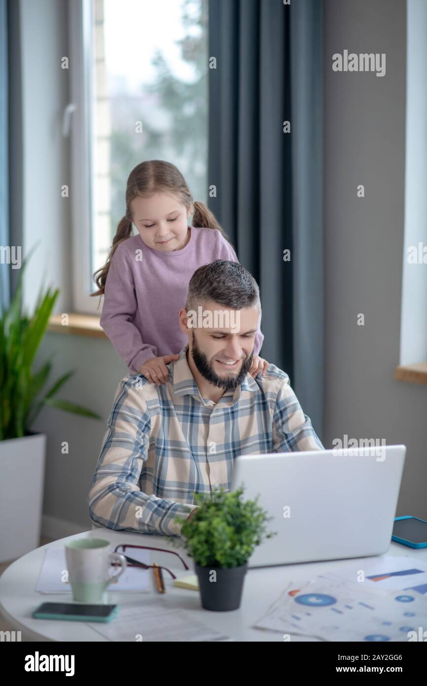Dad sitting working at laptop, little daughter behind daddys back Stock ...