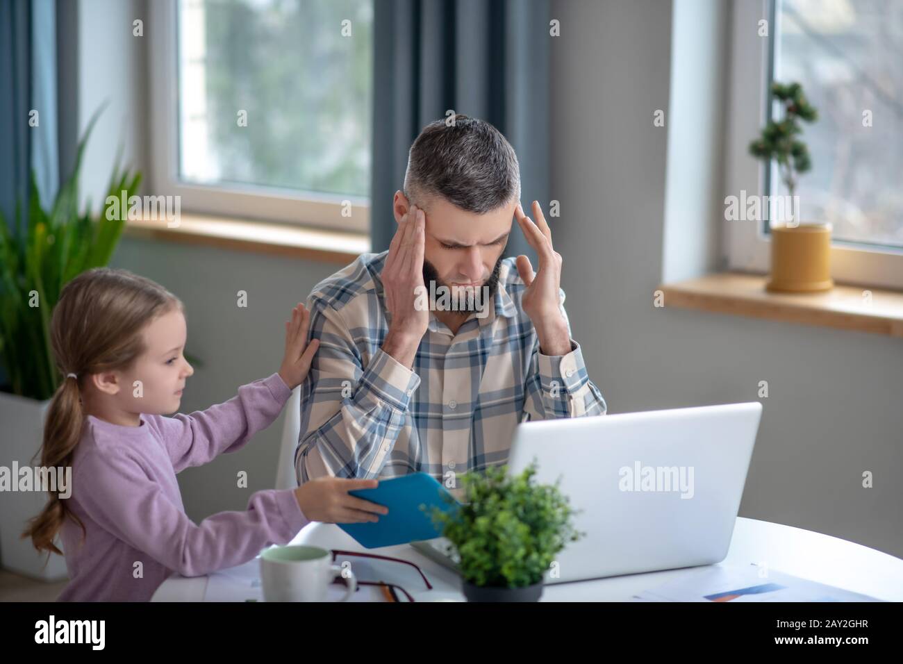 Tired dad sitting at laptop covering his eyes and daughter Stock Photo ...