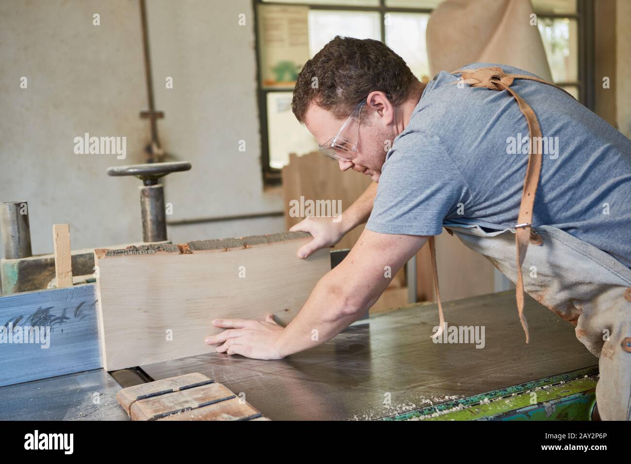 Carpenter in training with wood plank on the planing machine in the ...