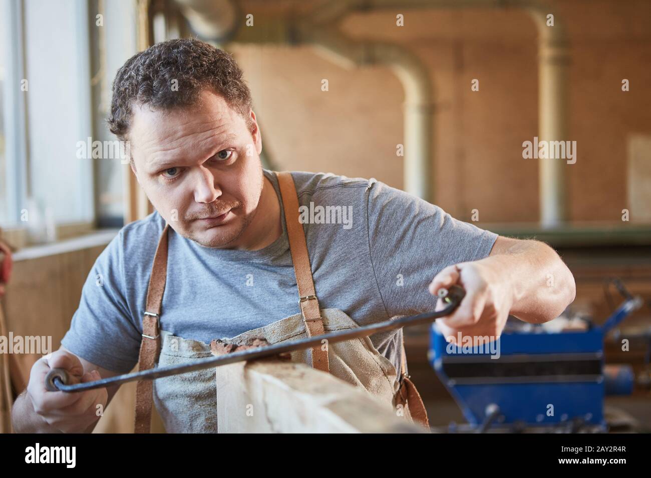 Carpenter apprentice in woodworking debarks wood with the tension knife ...