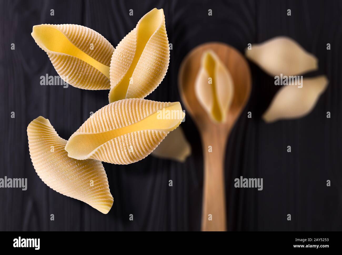 Top view of conchiglie pasta shells on black wooden table with spoon ...