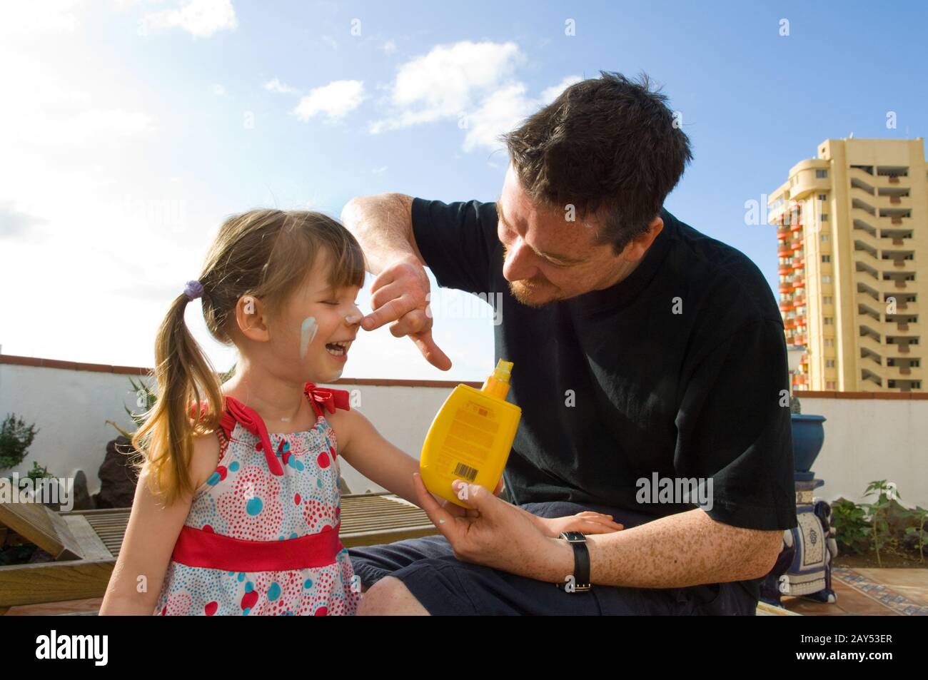 a father applying sun cream, sunscreen, to his daughters face to help ...