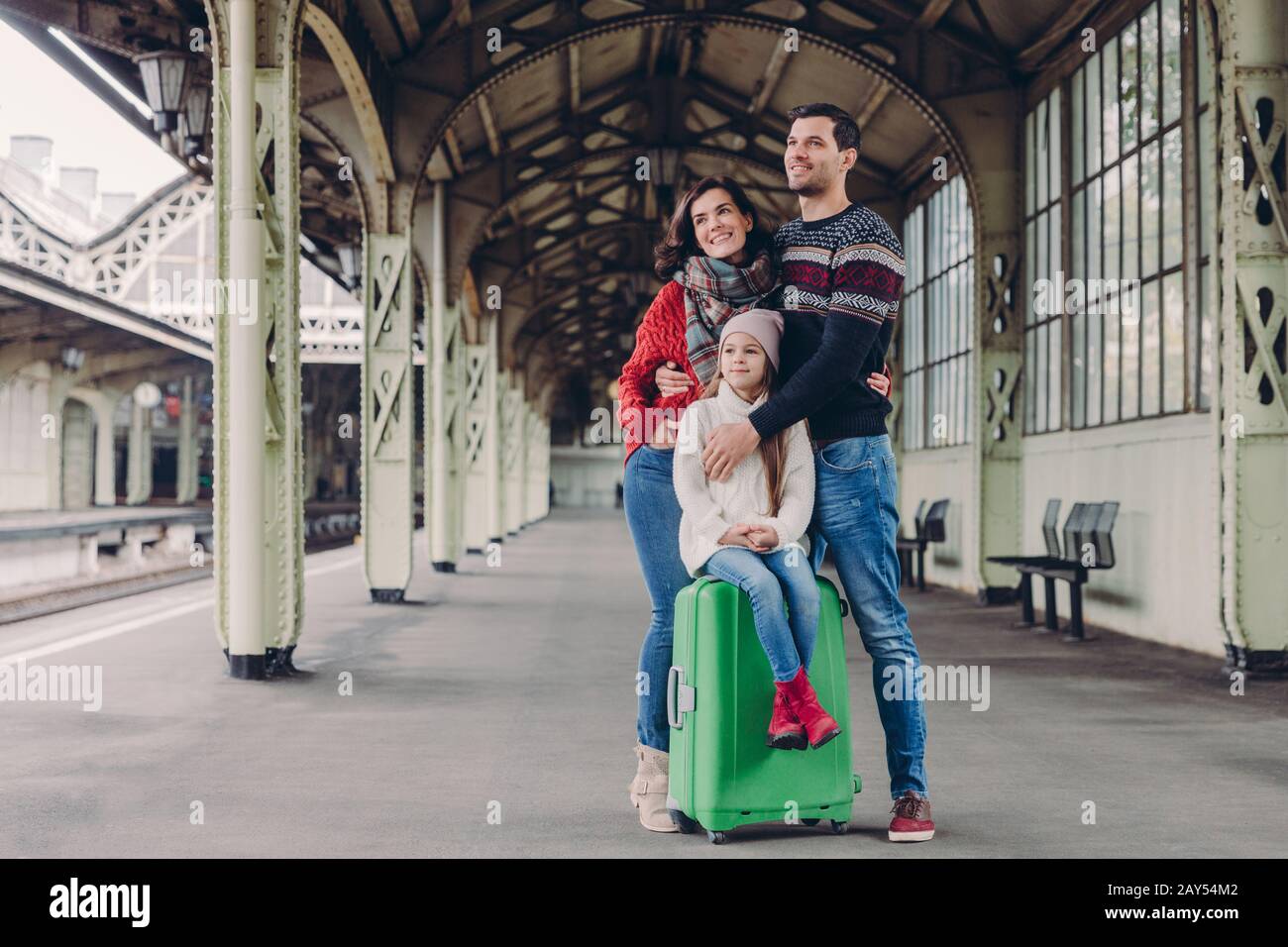 Pleased wife and husband cuddle with love, their daughter sits at ...