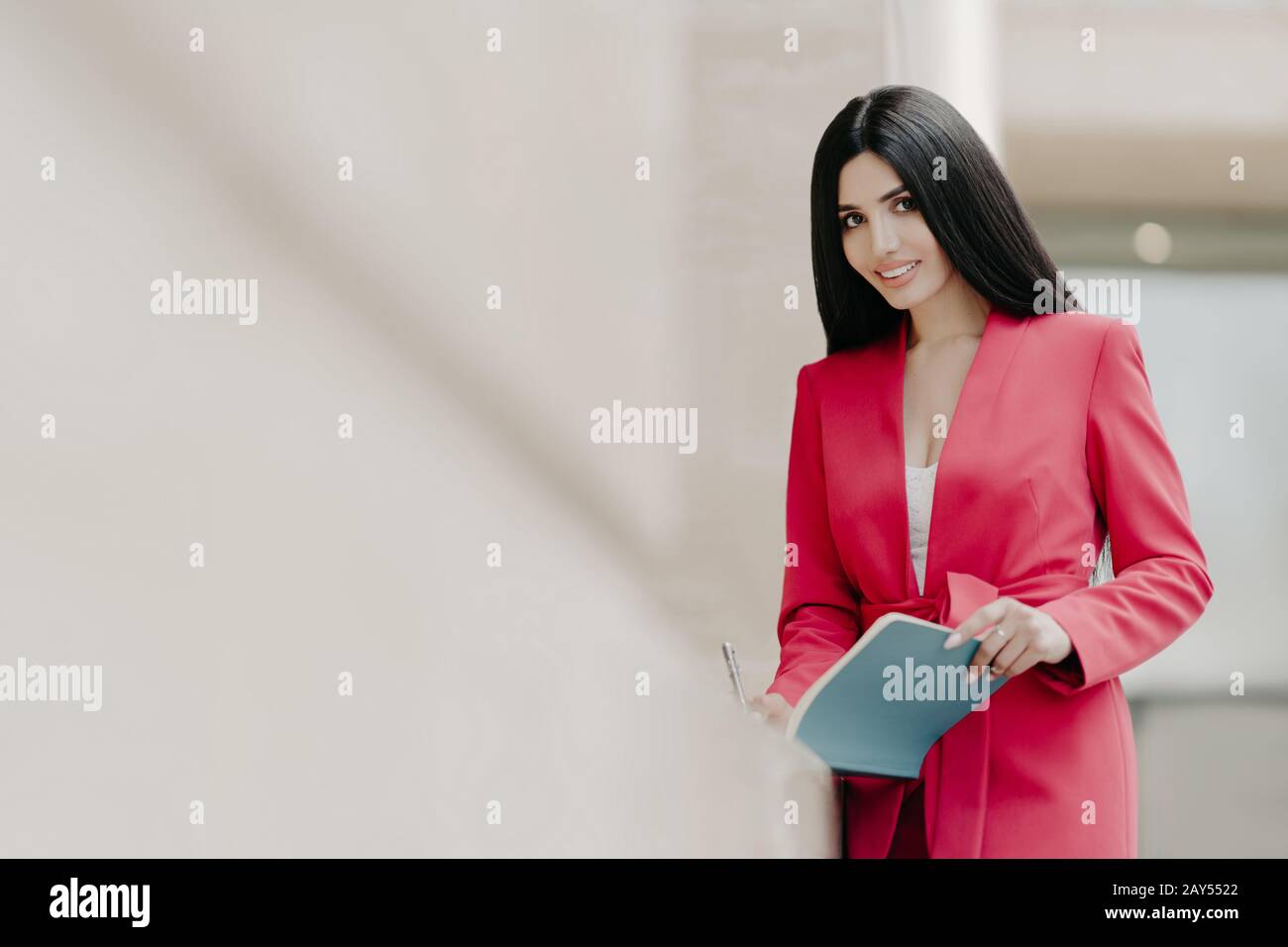 Beautiful smiling lady in elegant red costume, writes some notes in ...
