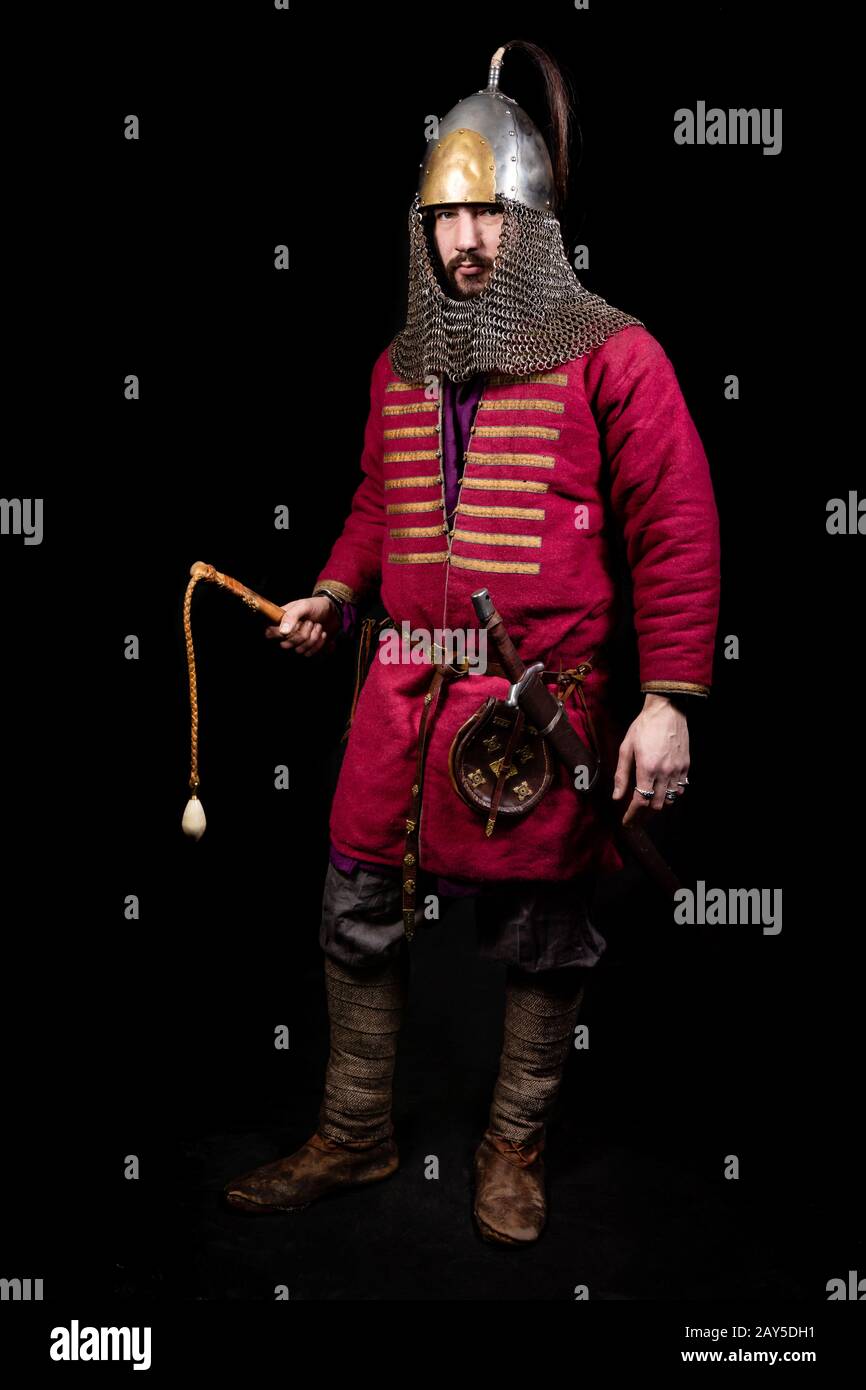 Slavic medieval warrior in a red coat and helmet holds a weapon in his ...