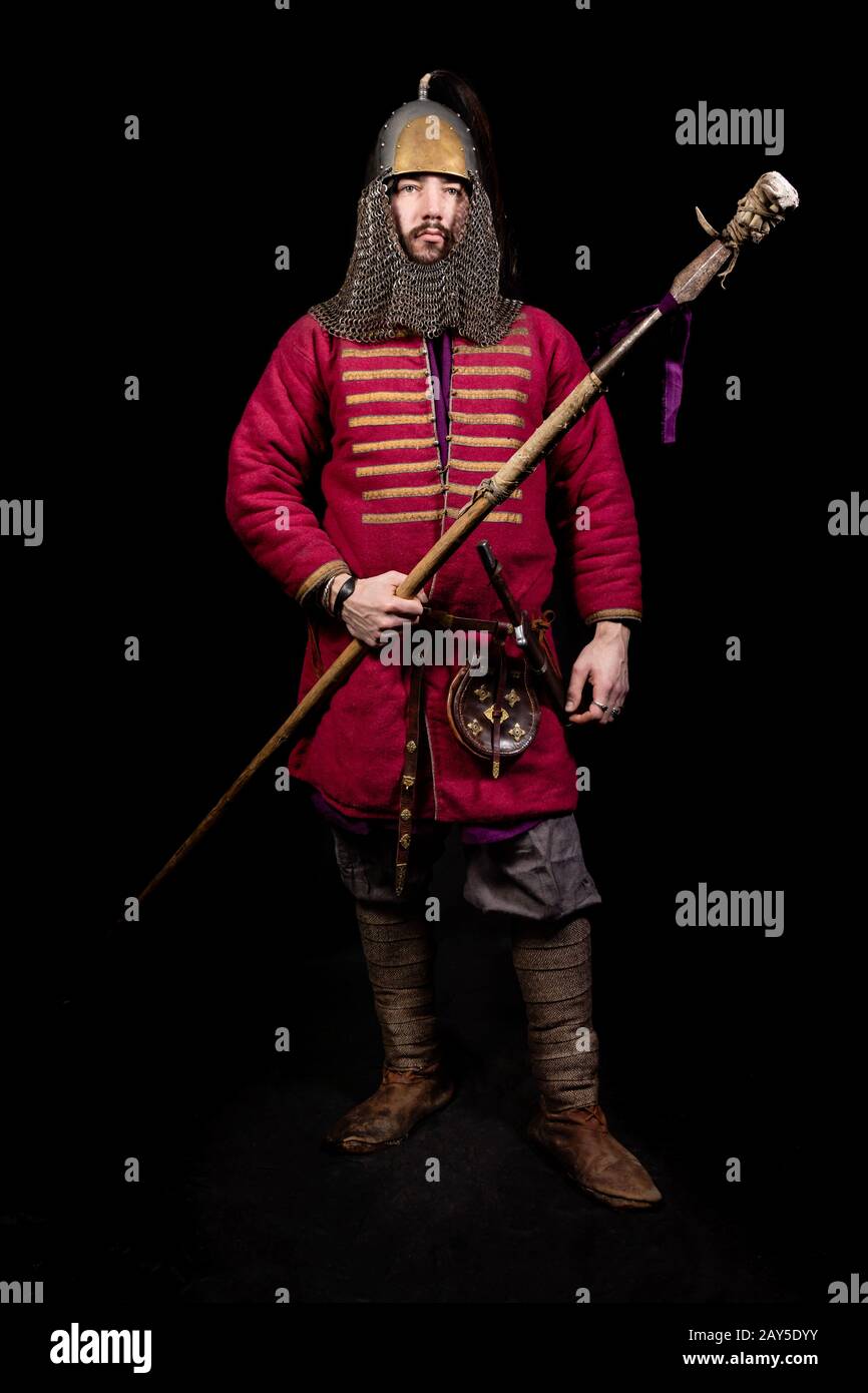 Slavic medieval warrior in a red coat and helmet holds a weapon in his ...