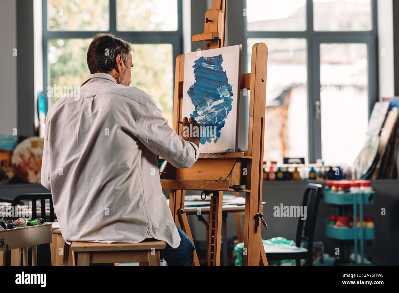 Back view of male painter drawing abstract picture on canvas while ...