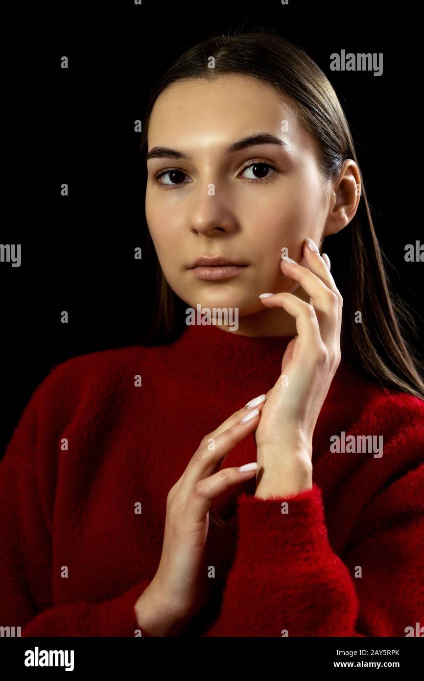 Girl in a red sweater. Hands near the face. Portrait of a timid girl on ...