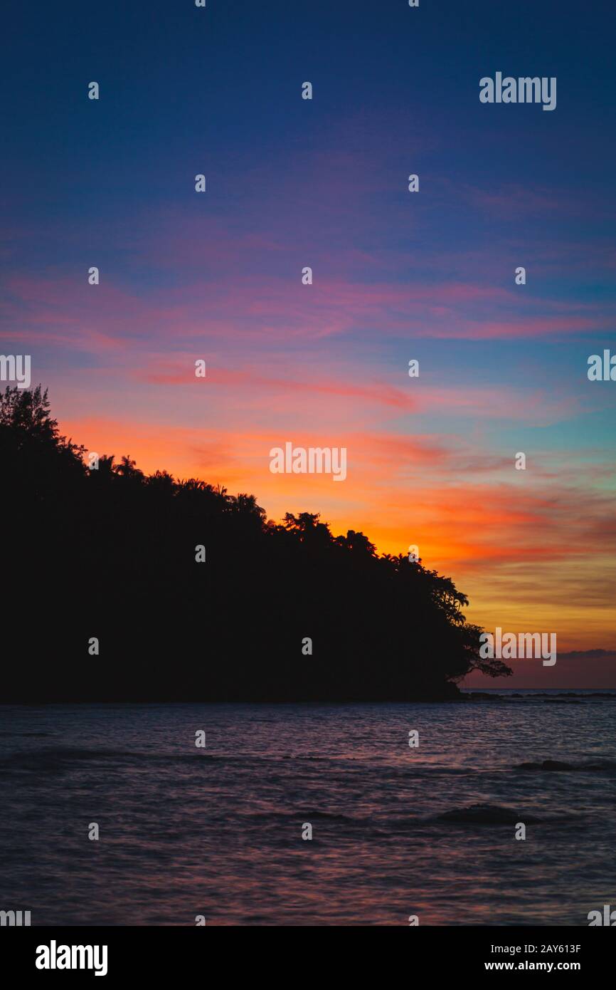 Vivid sunset sky waterscape and silhouette forest island background ...