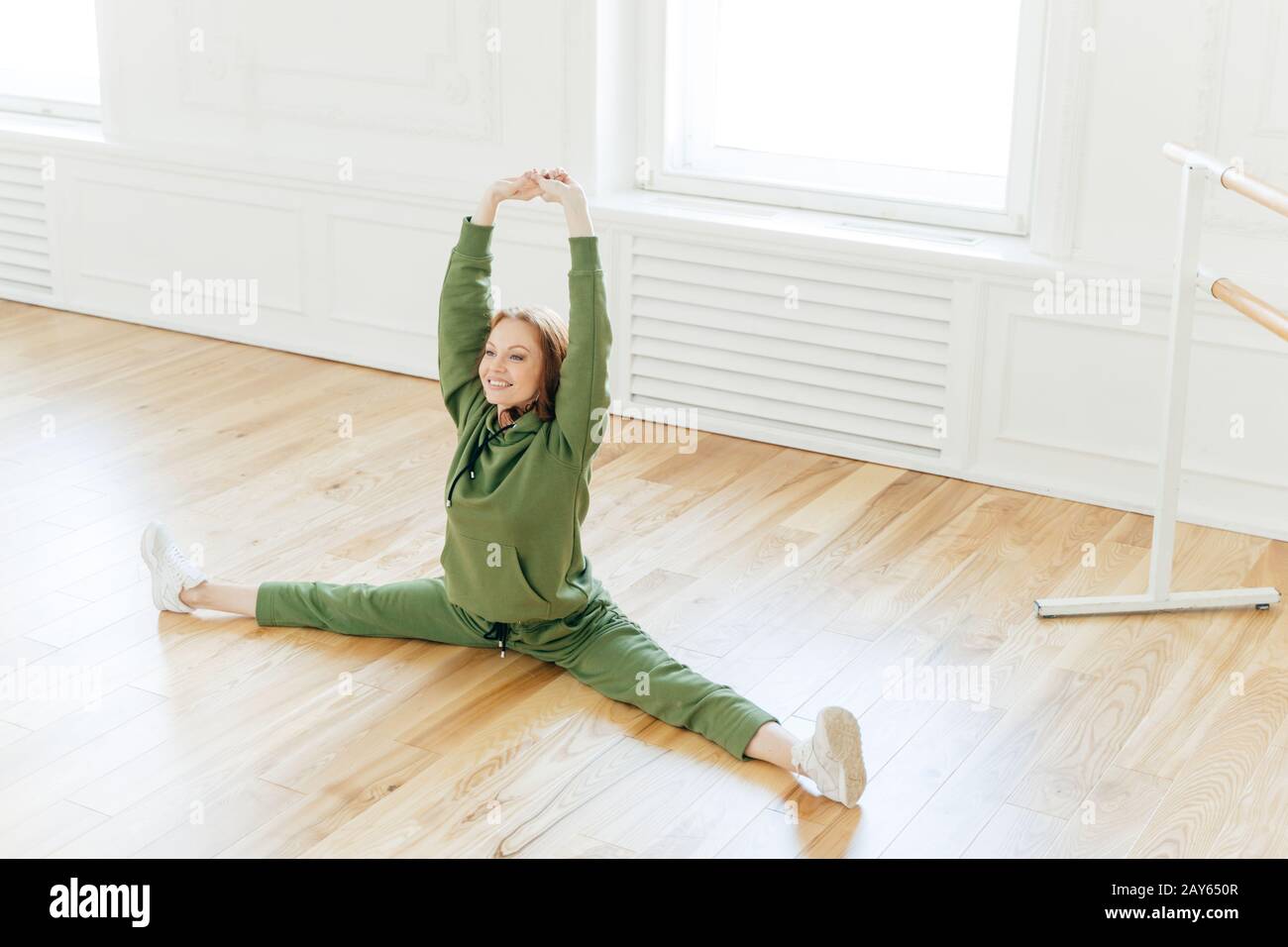 Strong flexible curly red haired woman does side leg split, raises ...