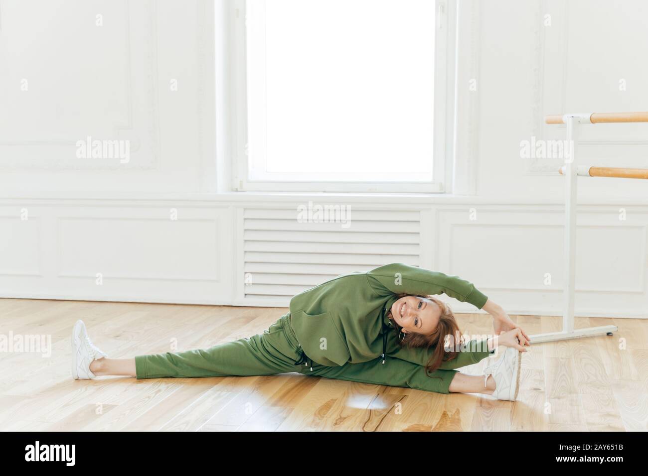 Photo of young slim gymnast does leg split, tilts body to right ...