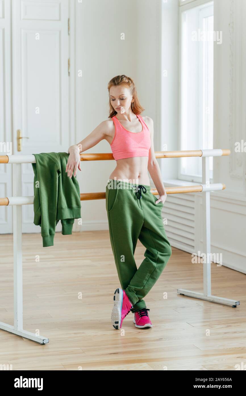 Beautiful fit ginger female dancer has rest near barre in ballet ...