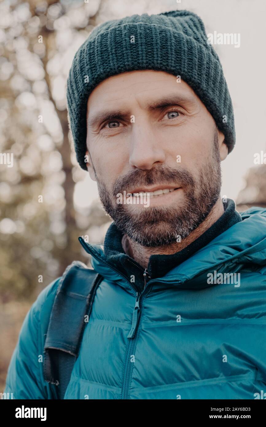 Close up shot of blue eyed man has dark bristle, looks seriously at ...
