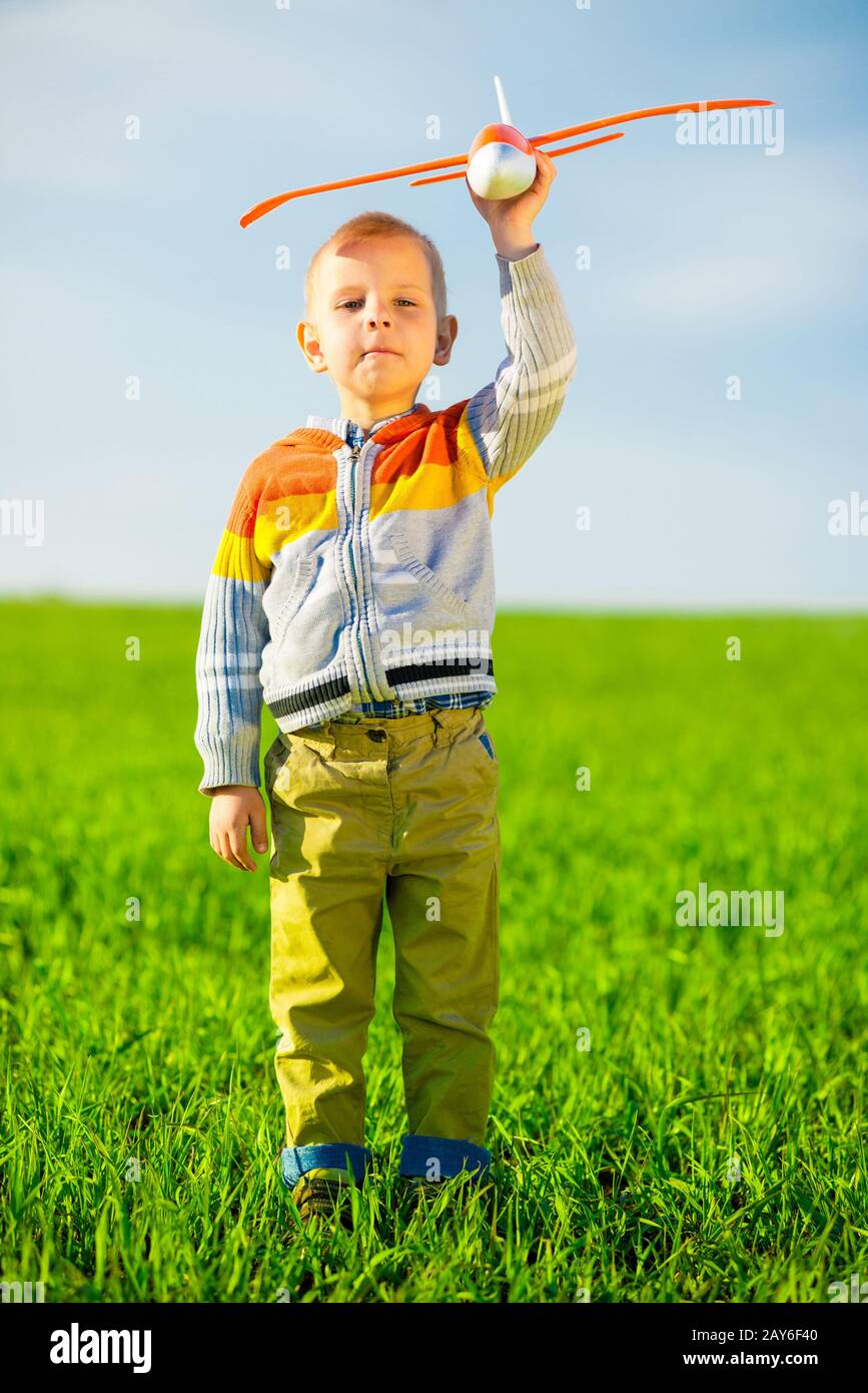 Happy boy playing with toy airplane against blue summer sky and green ...