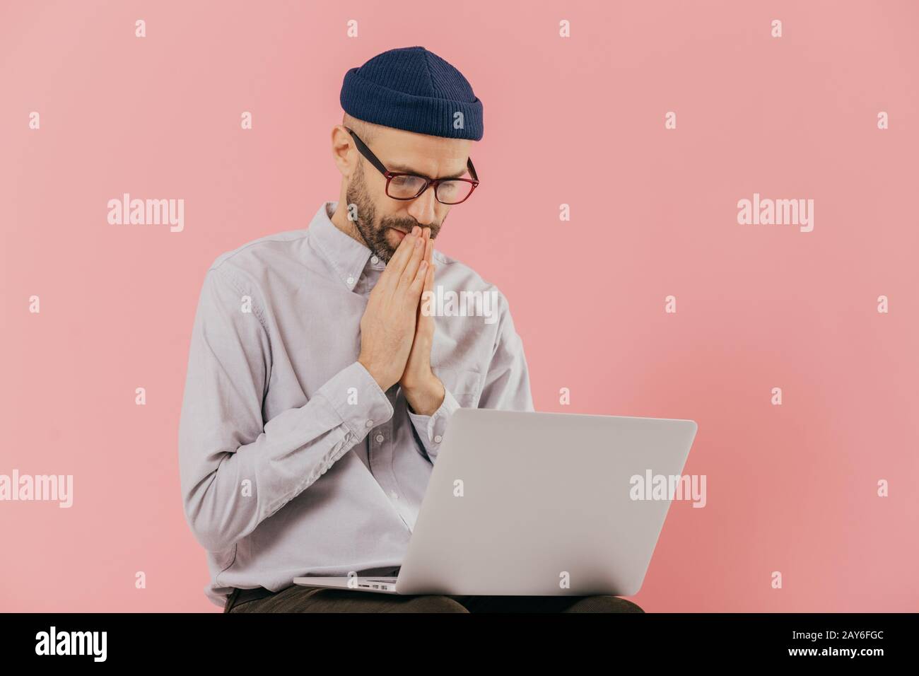 Professional male programmer keeps hans in praying gesture, looks at ...