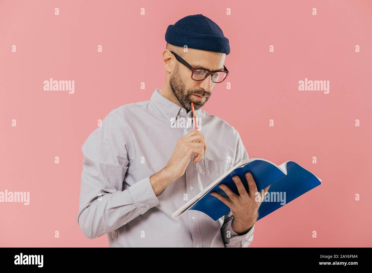 Photo of handsome male author has dark bristle, holds pencil and book ...