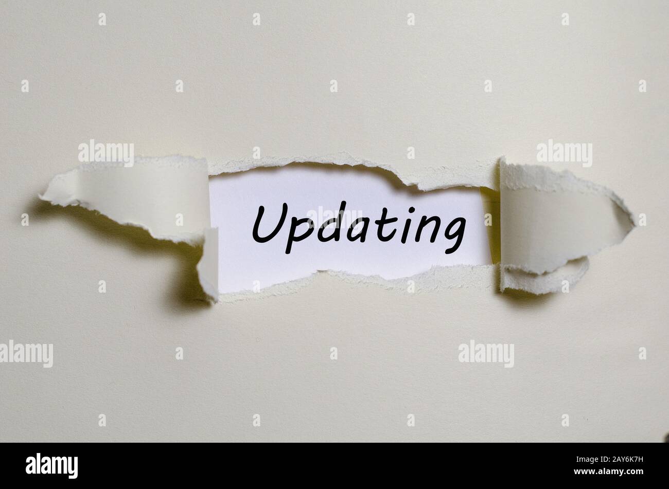 The word updating appearing behind torn paper Stock Photo - Alamy