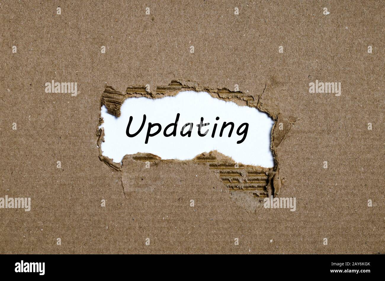 The word updating appearing behind torn paper Stock Photo - Alamy