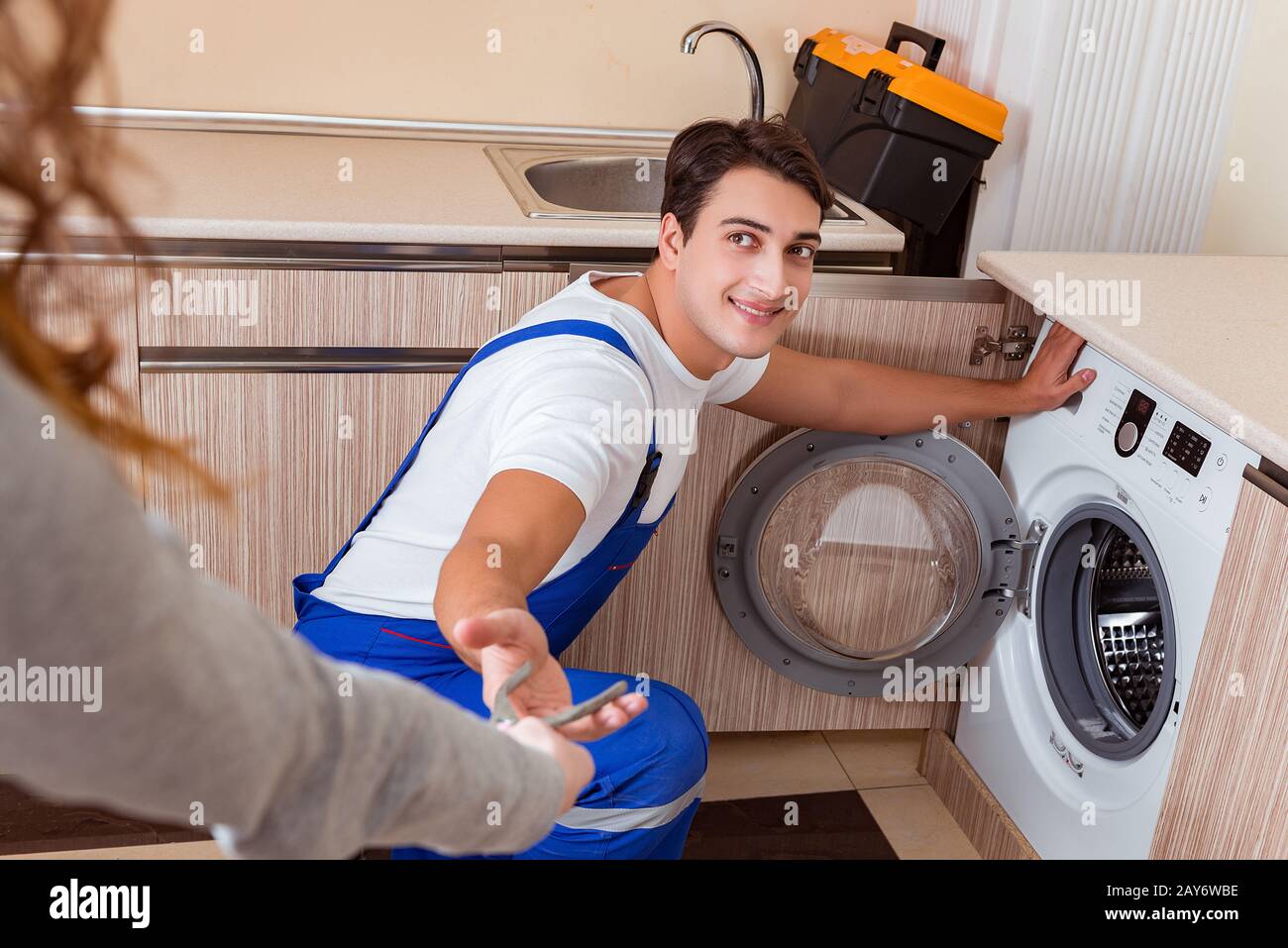 Repairman repairing washing machine at kitchen Stock Photo - Alamy
