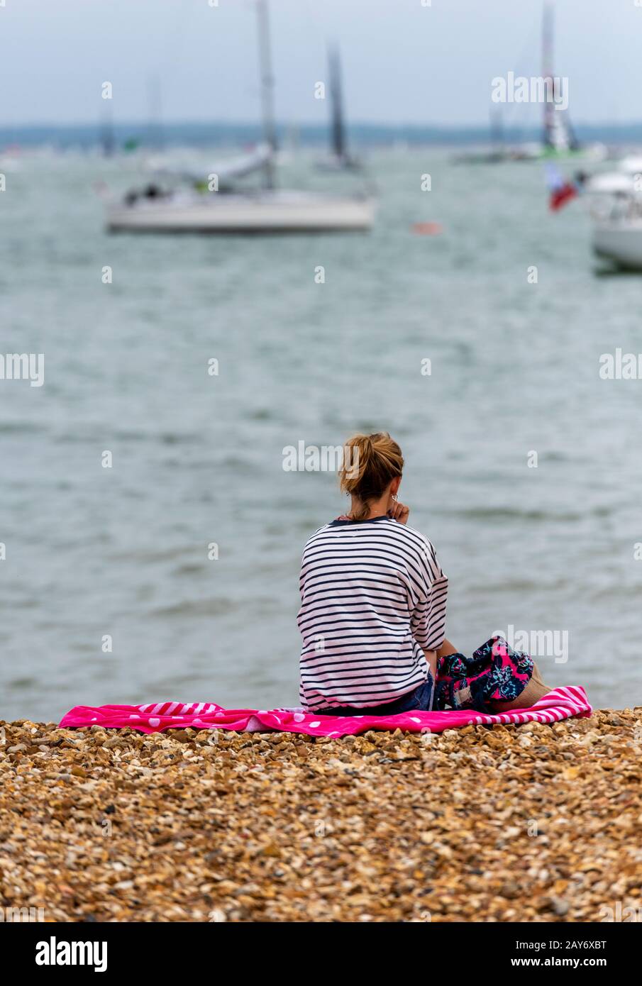 a young woman sitting on a beach watching the yachts at cowes on the ...