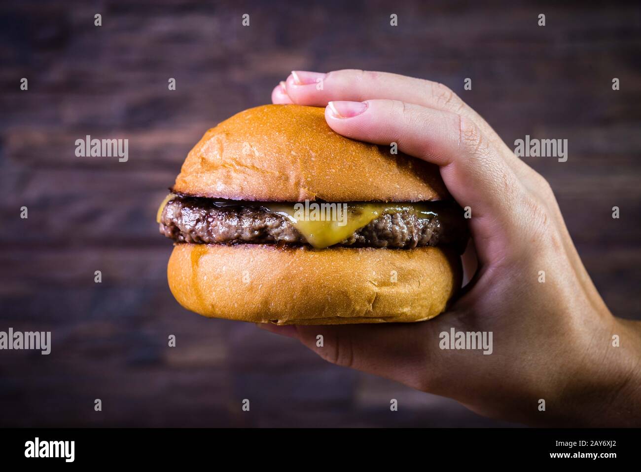 Hand holding a craft beef burger with cheese on rustic background Stock ...