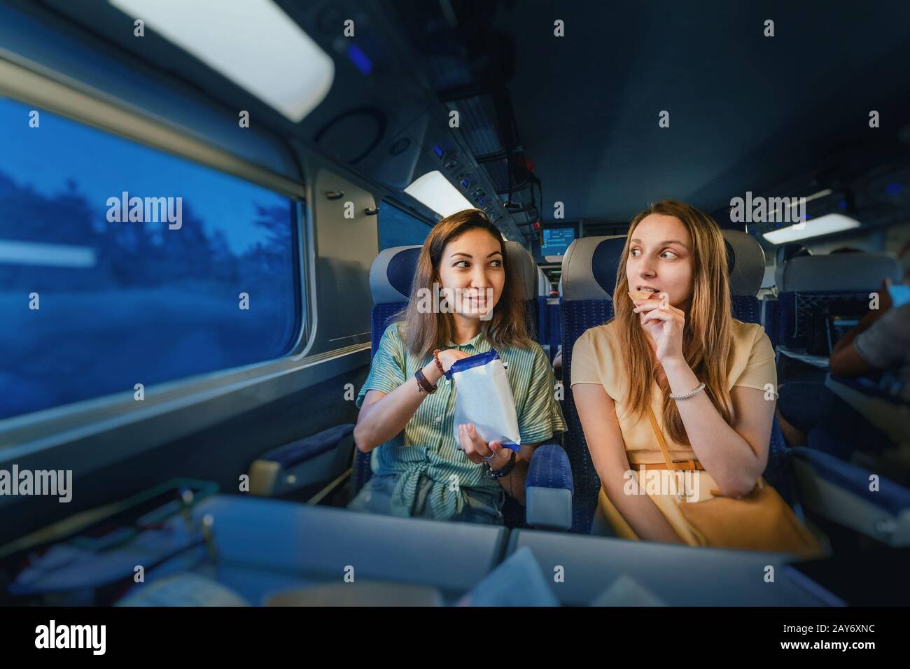 Two girl friends passengers sitting in first class train at night time ...