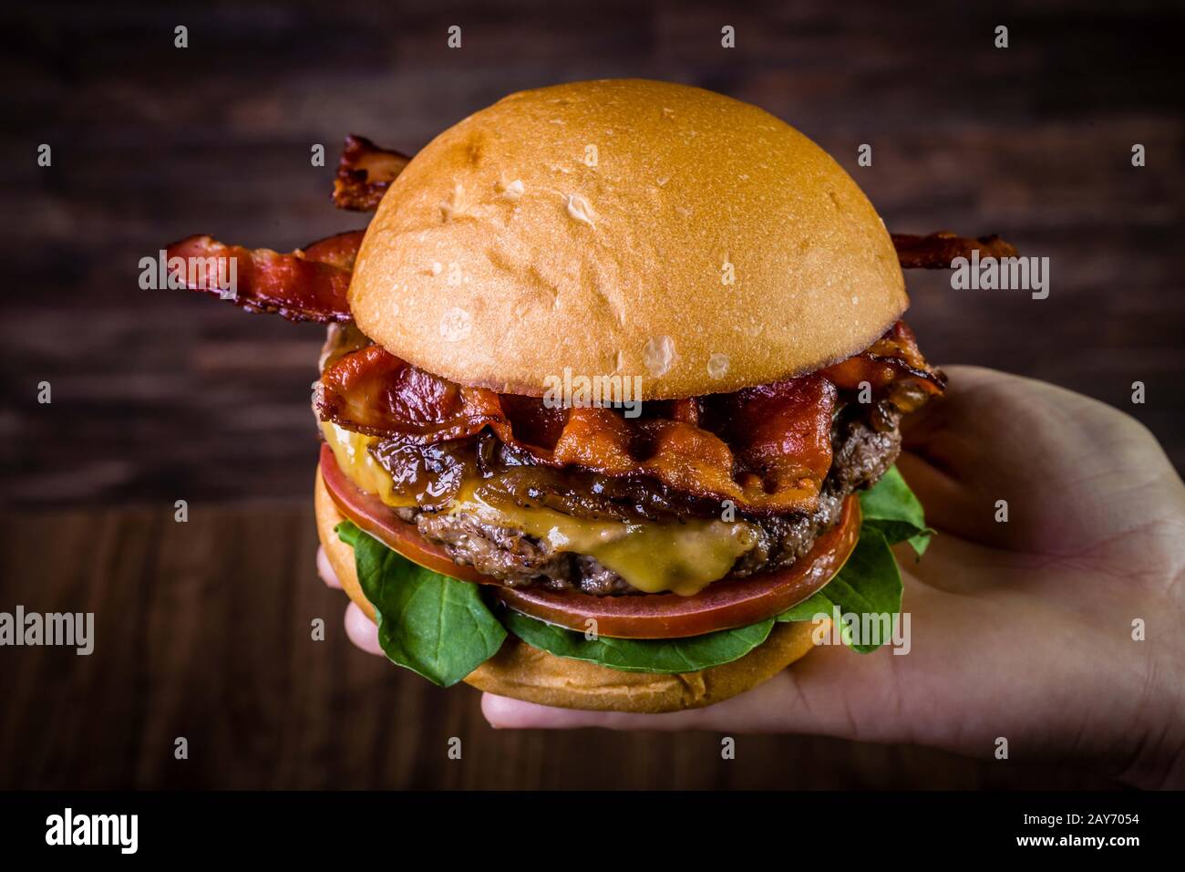 Hand holding a craft beef burger with cheese, bacon, caramelized onion ...