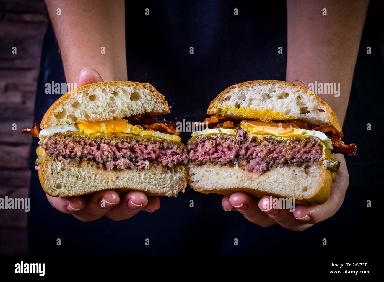 Hand holding a splited craft beef burger with cheese, egg, bacon and ...