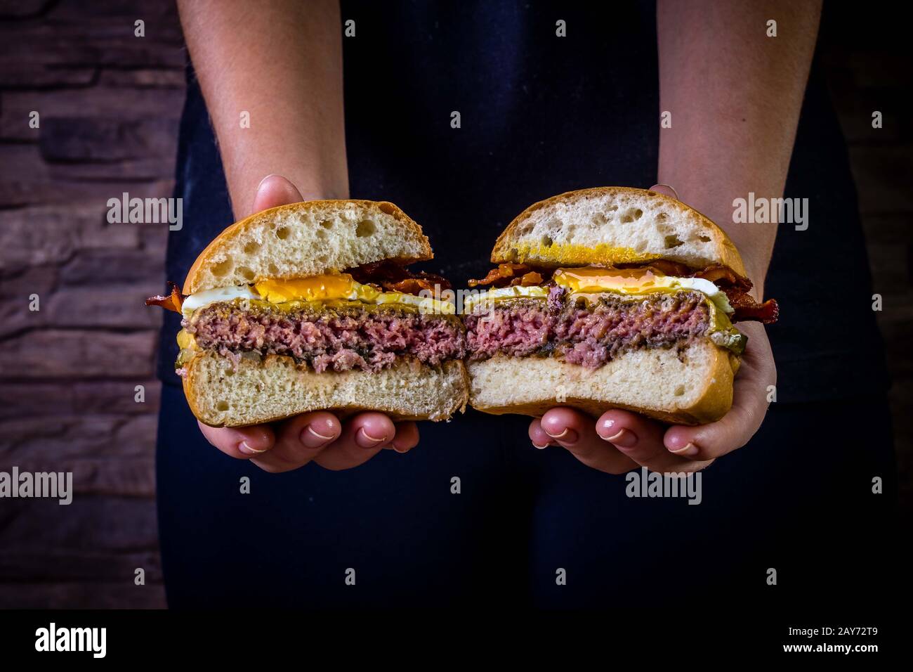 Hand holding a splited craft beef burger with cheese, egg, bacon and ...