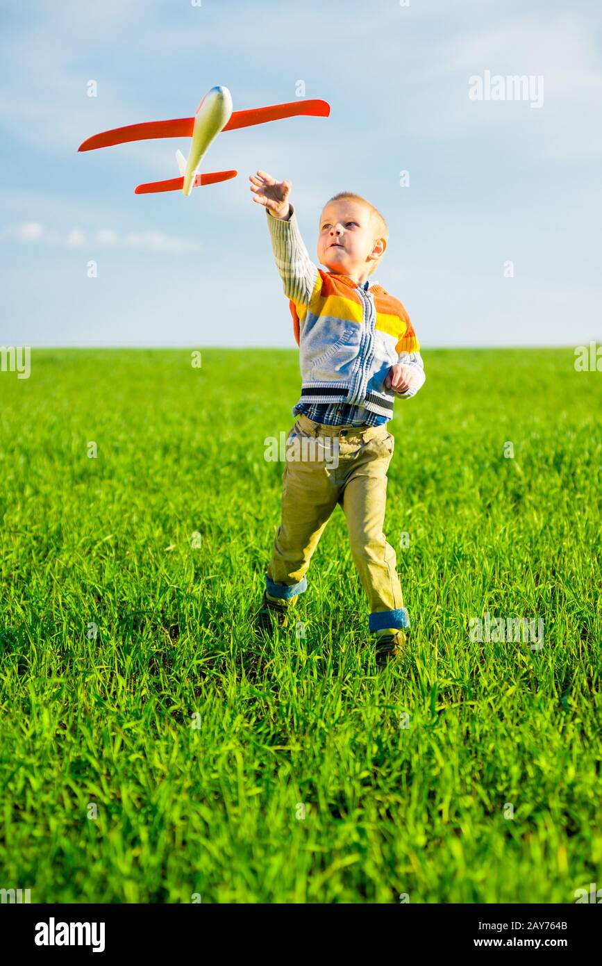 Happy boy playing with toy airplane against blue summer sky and green ...