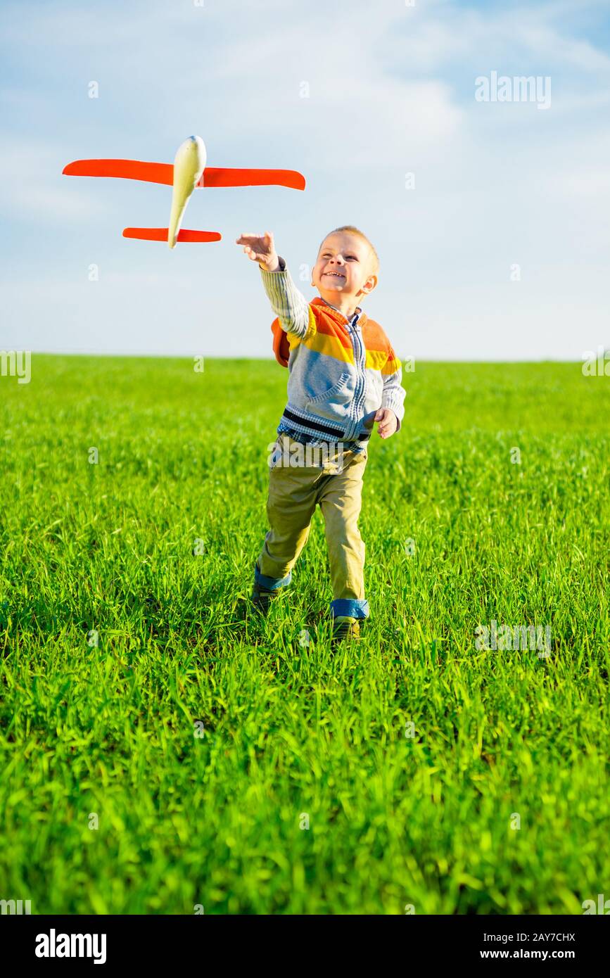 Happy boy playing with toy airplane against blue summer sky and green ...